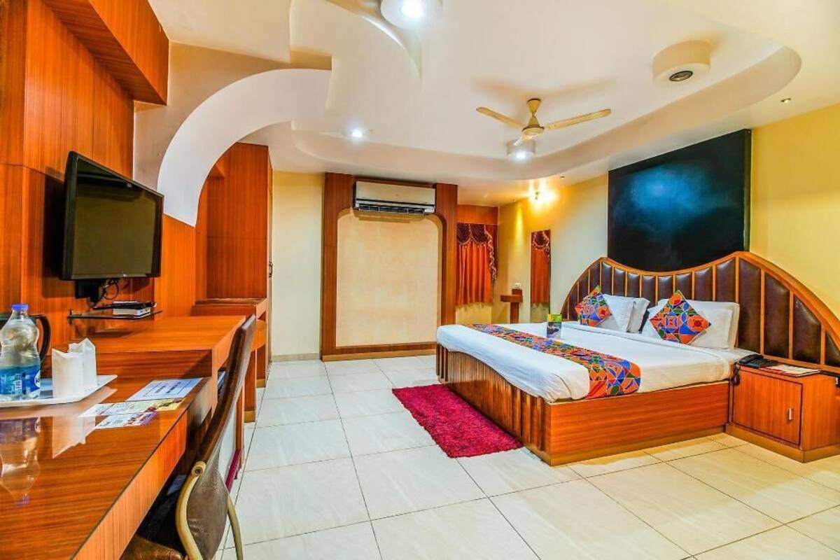 Quarto de hotel com escrivaninha de madeira, cama com cabeceira, ventoinha no teto, aparelho de ar condicionado e televisão.