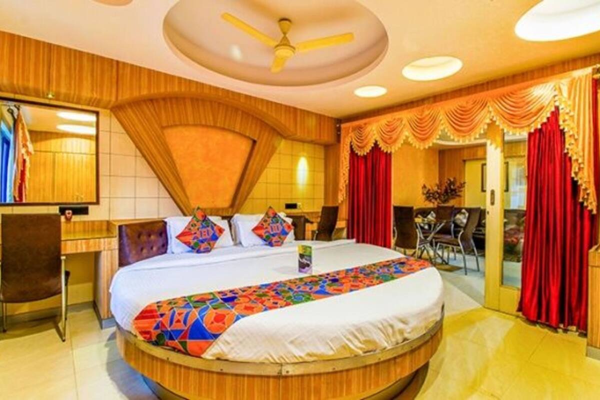 Quarto de hotel com uma cama grande, um ventilador de teto, uma área de refeições com cortinas vermelhas e vista para o exterior.