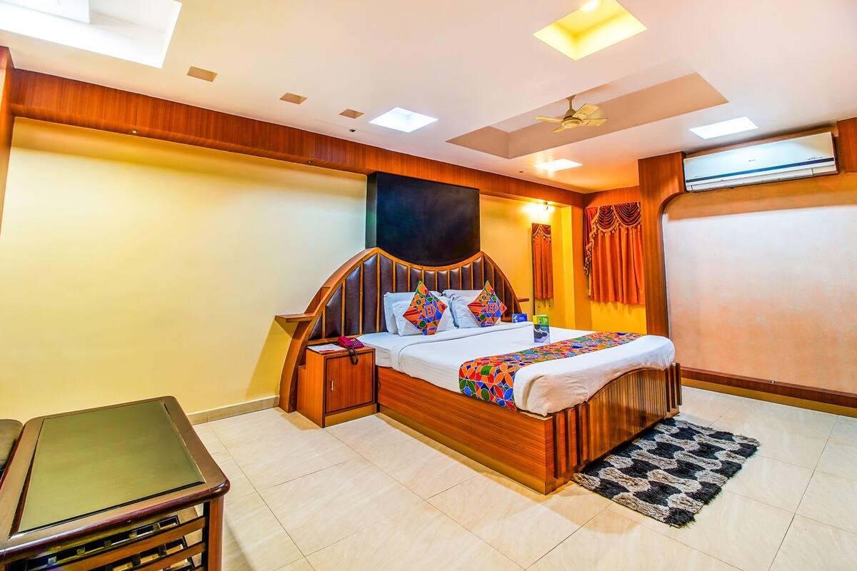Quarto com cama de madeira, mesa de cabeceira, pequena mesa e ventilador de teto.
