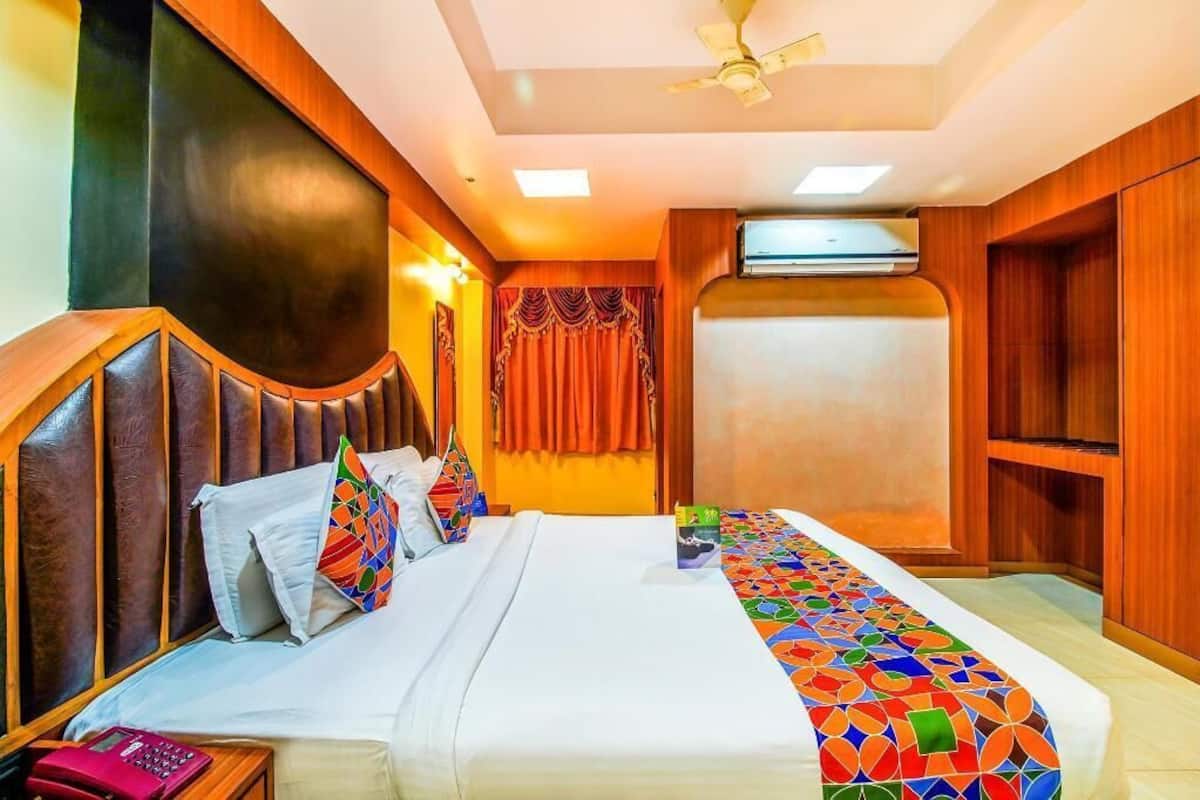 Quarto de hotel com cama, mesa de cabeceira, ventilador de teto, ar condicionado e janela com cortinas.