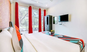 Quarto de hotel com cama, escrivaninha, televisão e janela com cortinas vermelhas.