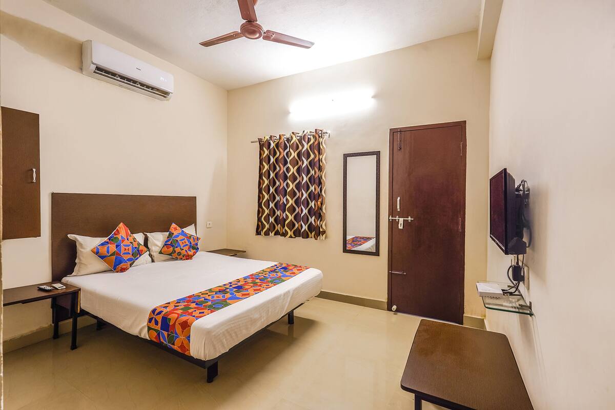 Quarto de hotel com cama, mesa de cabeceira, armário, televisão e ar condicionado.