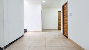 Um corredor com piso de azulejos, paredes brancas e porta de madeira com placa de identificação.