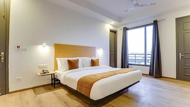 Quarto de hotel com uma cama grande, uma mesa de cabeceira, um ventilador de teto e uma janela com cortinas.