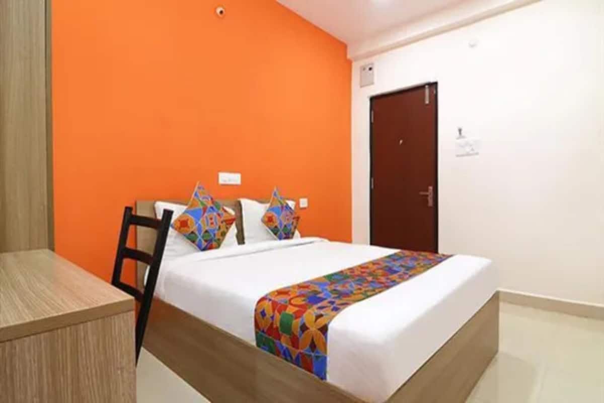 Quarto de hotel com parede laranja, cama com manta colorida, secretária de madeira e uma porta.