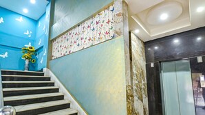 Uma escadaria com um vaso de girassóis, uma parede com desenhos de borboletas e um elevador.