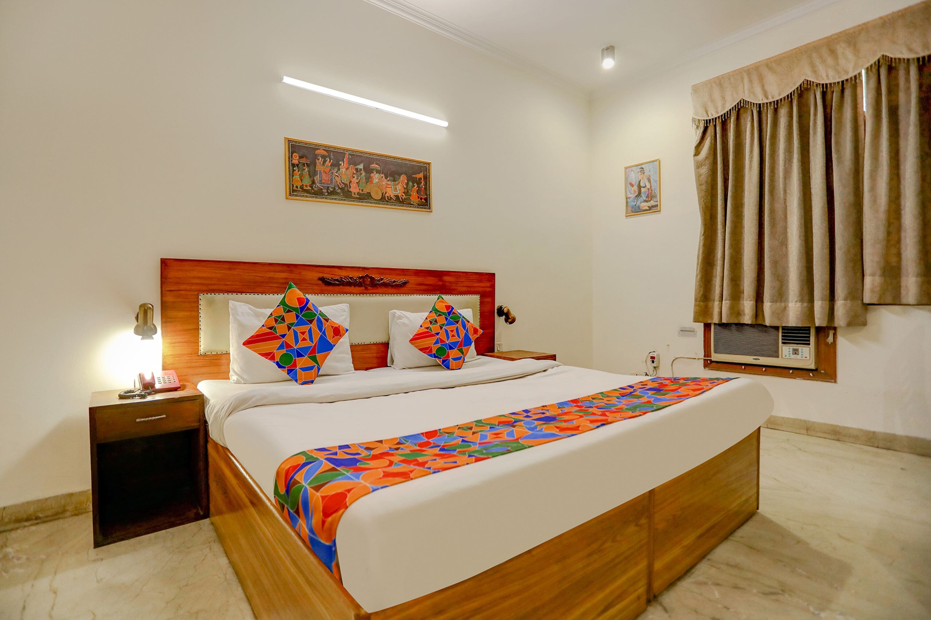 Quarto de hotel com cama de madeira, mesa de cabeceira com telefone, ar condicionado fixado na parede e um quadro sobre a cama.