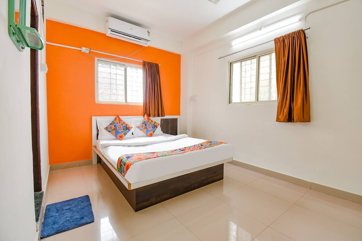 Um quarto com uma parede laranja, uma cama com colcha estampada e um tapete azul no chão.