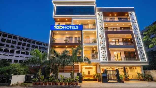 Um edifício moderno de vários andares com um destaque para a placa 'fabHOTELS', varandas e plantas em vasos.