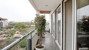 Uma varanda com planta em vaso, porta de vidro e vista para a paisagem urbana.