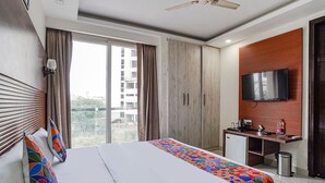 Quarto de hotel com cama, escrivaninha, televisão e varanda com cortinas.