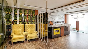 Uma área de recepção de hotel com piso de mármore, um balcão de atendimento com a placa 'fab hotels' e poltronas amarelas.