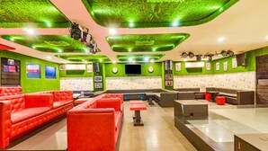 Uma sala de estar moderna com assentos verdes e vermelhos, uma TV de tela plana e um jukebox.