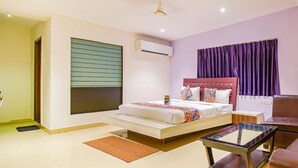 Quarto de hotel moderno com uma cama, um sofá, uma mesinha e uma janela com cortinas roxas.