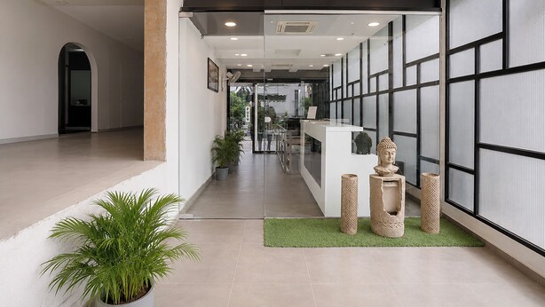 Um lobby de hotel moderno com uma mesa de recepção, plantas em vasos e um tapete verde.