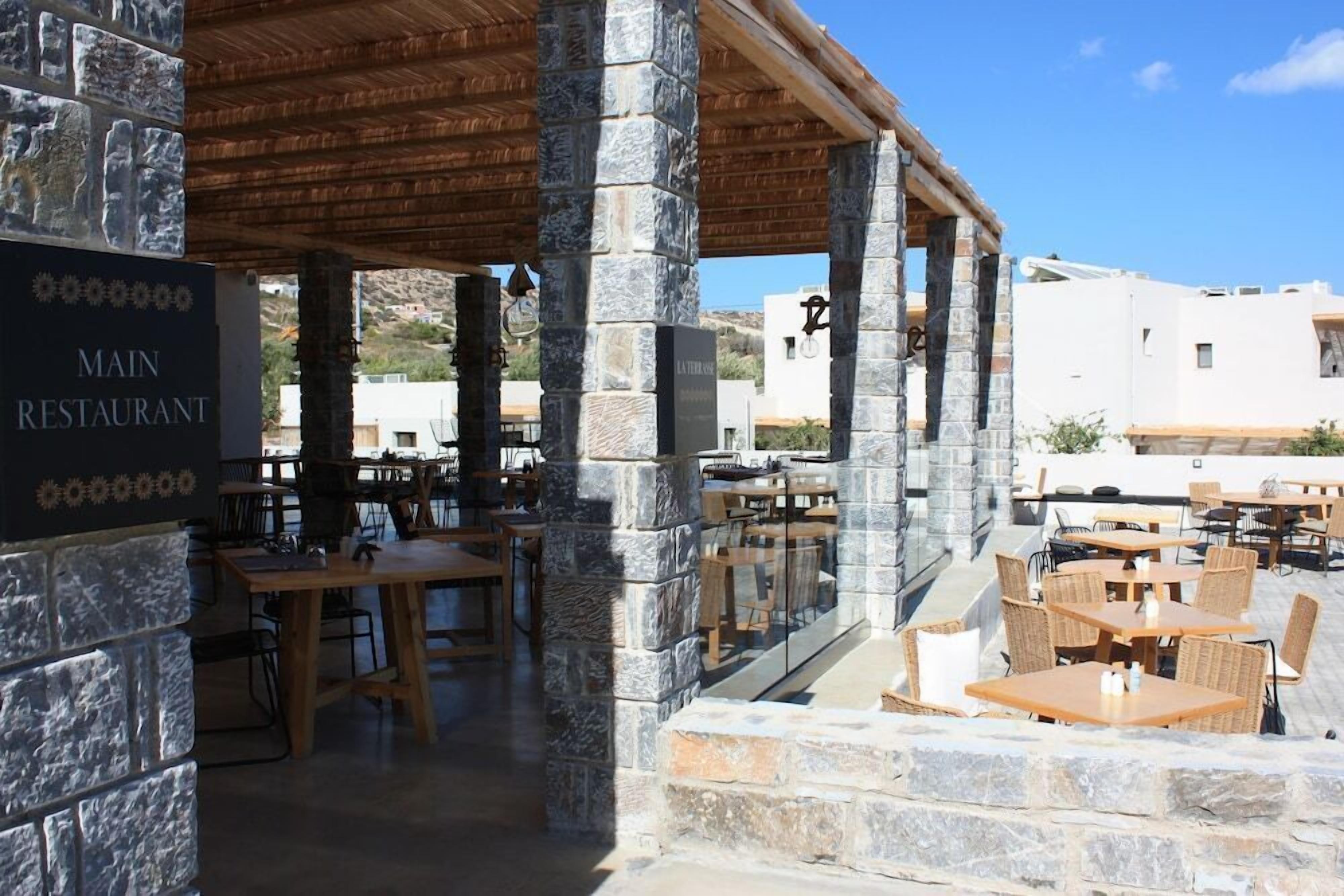 Restaurante ao ar livre com pilares de pedra, mesas de madeira e placa indicando ser o restaurante principal.