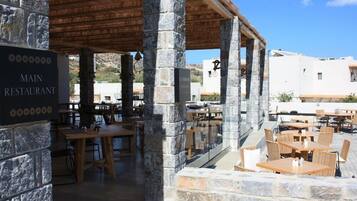 Restaurante ao ar livre com pilares de pedra, mesas de madeira e placa indicando ser o restaurante principal.