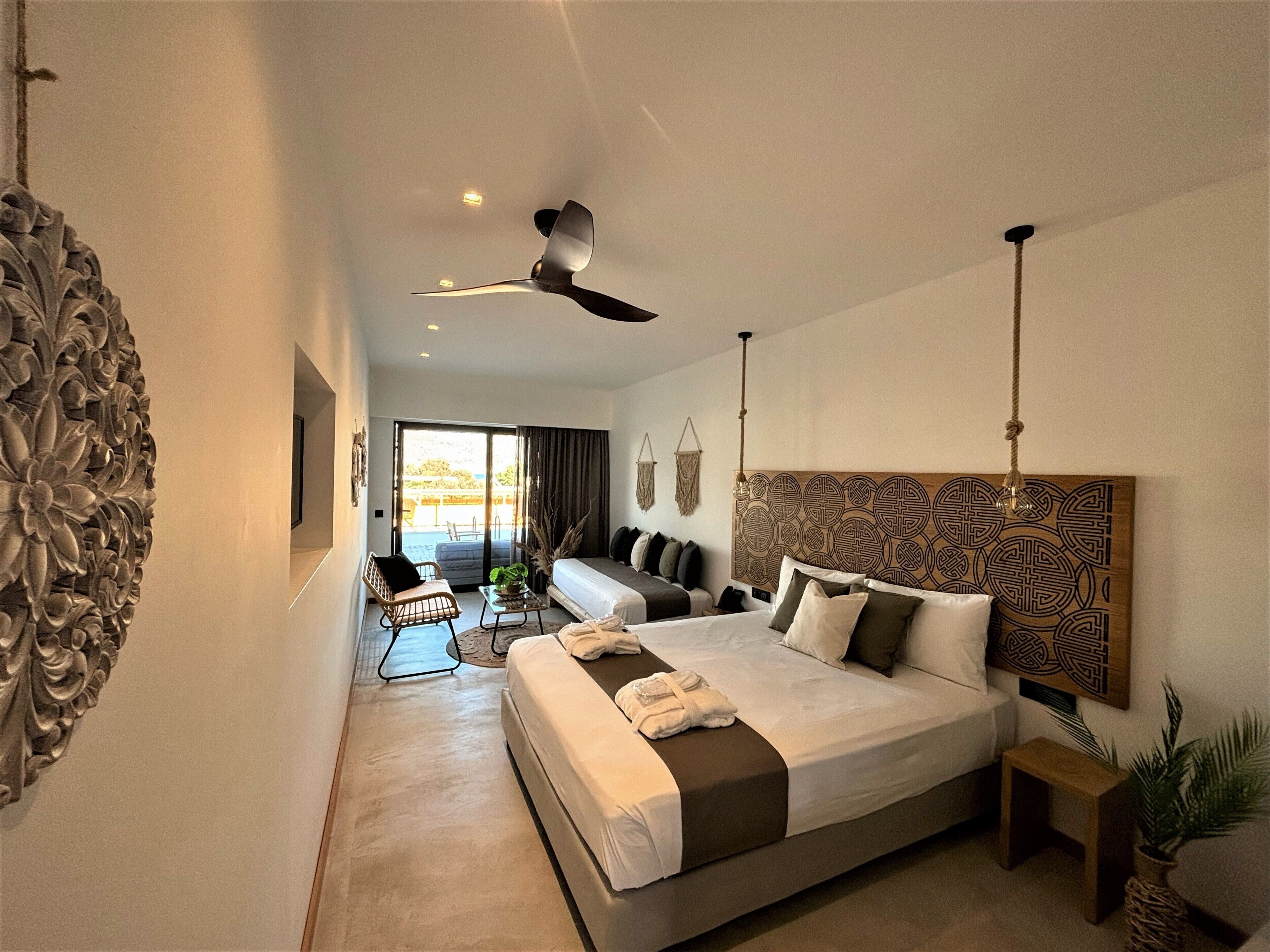 Quarto de hotel moderno com cama grande, área de estar e vista para o exterior.