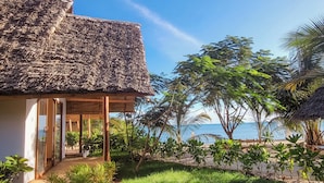 Uma casa com telhado de palha, porta de entrada em vidro e vista para o oceano.