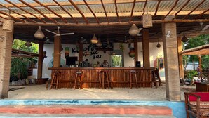 Um bar à beira-mar com estrutura de madeira, balcão e decorações penduradas.
