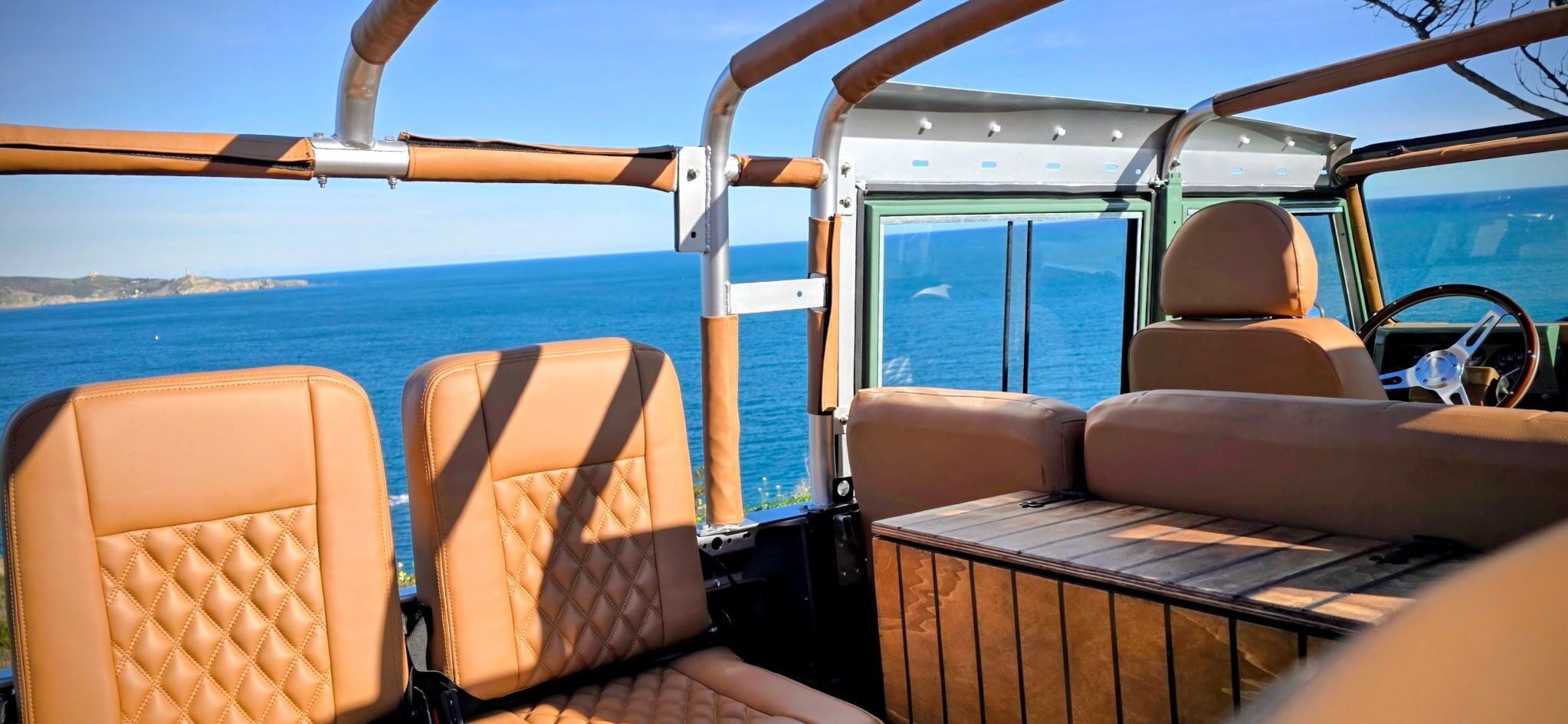 Interior de barco com dois assentos acolchoados, um volante e vista para o mar.