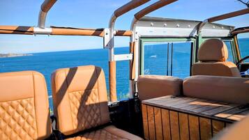 Interior de barco com dois assentos acolchoados, um volante e vista para o mar.