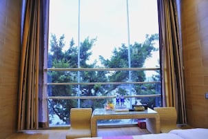 Quarto de hotel com uma grande janela, uma mesa pequena, duas cadeiras e uma cama.