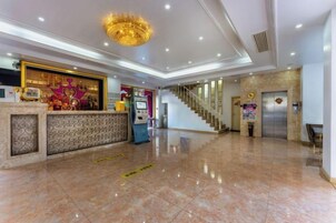 Um hall de hotel com balcão de recepção, escada e lustre moderno.
