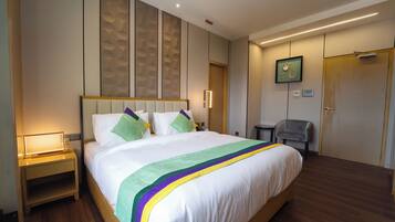 Quarto de hotel com uma cama grande, mesas de cabeceira, escrivaninha, cadeira e uma porta.