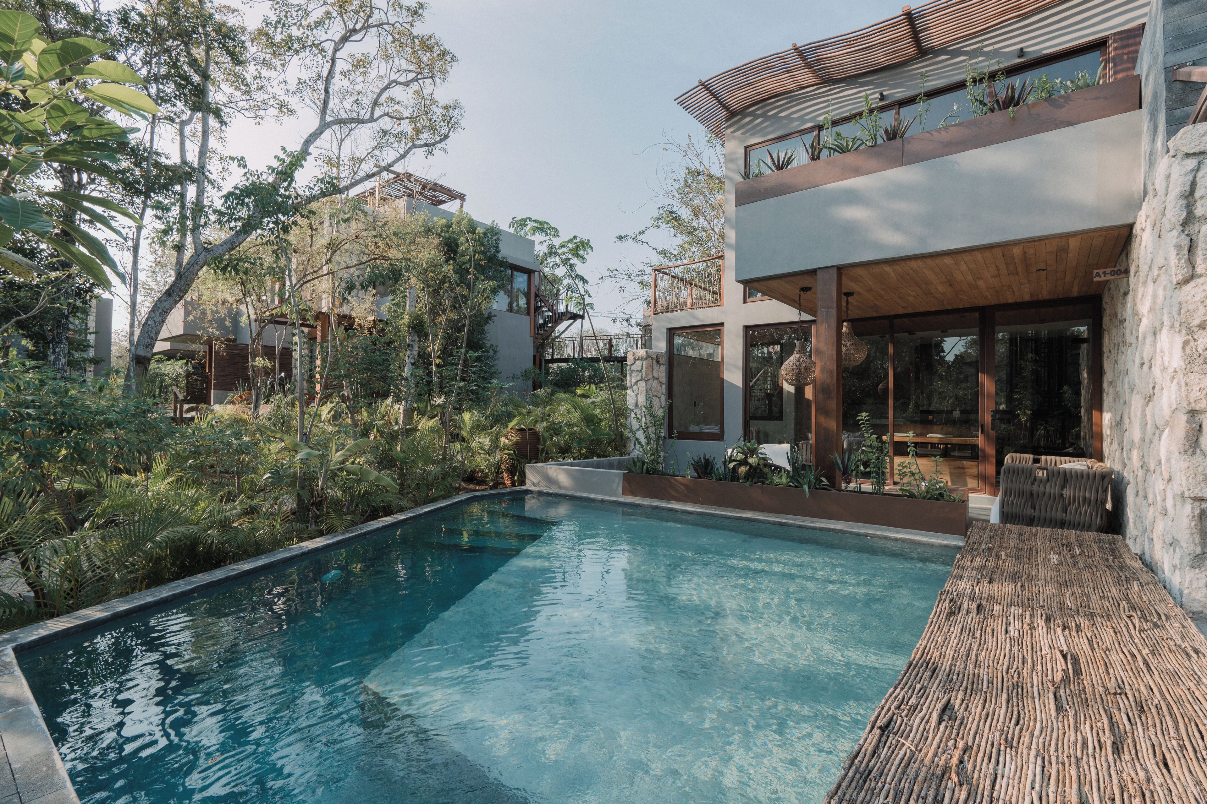Uma área de piscina moderna com piscina límpida, deck de madeira e vegetação ao redor.