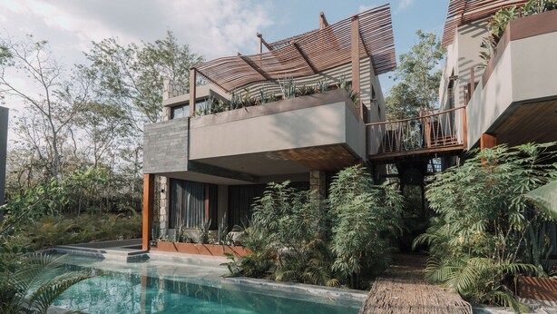 Um edifício moderno com um jardim no terraço, piscina e muita vegetação.