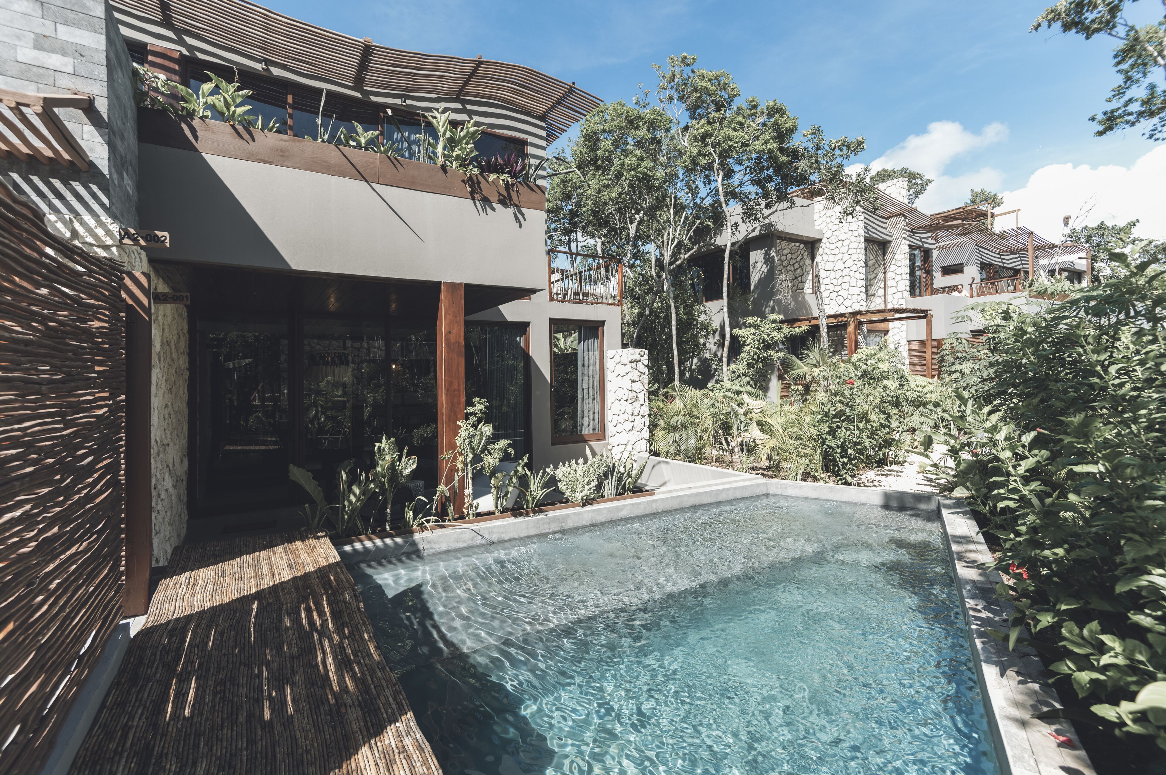Um resort moderno com piscina, paredes de pedra e vegetação exuberante.