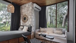 Um quarto aconchegante com parede de pedra, um sofá cinza, uma cadeira preta e uma mesinha.