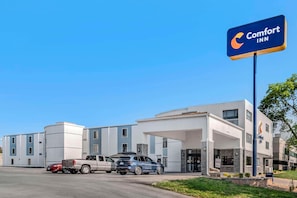 Um hotel Comfort Inn com design moderno, um estacionamento com vários veículos e um céu azul claro.