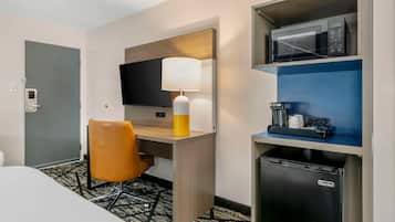 Quarto de hotel com cama, escrivaninha com luminária, televisão, micro-ondas, máquina de café e mini-geladeira.