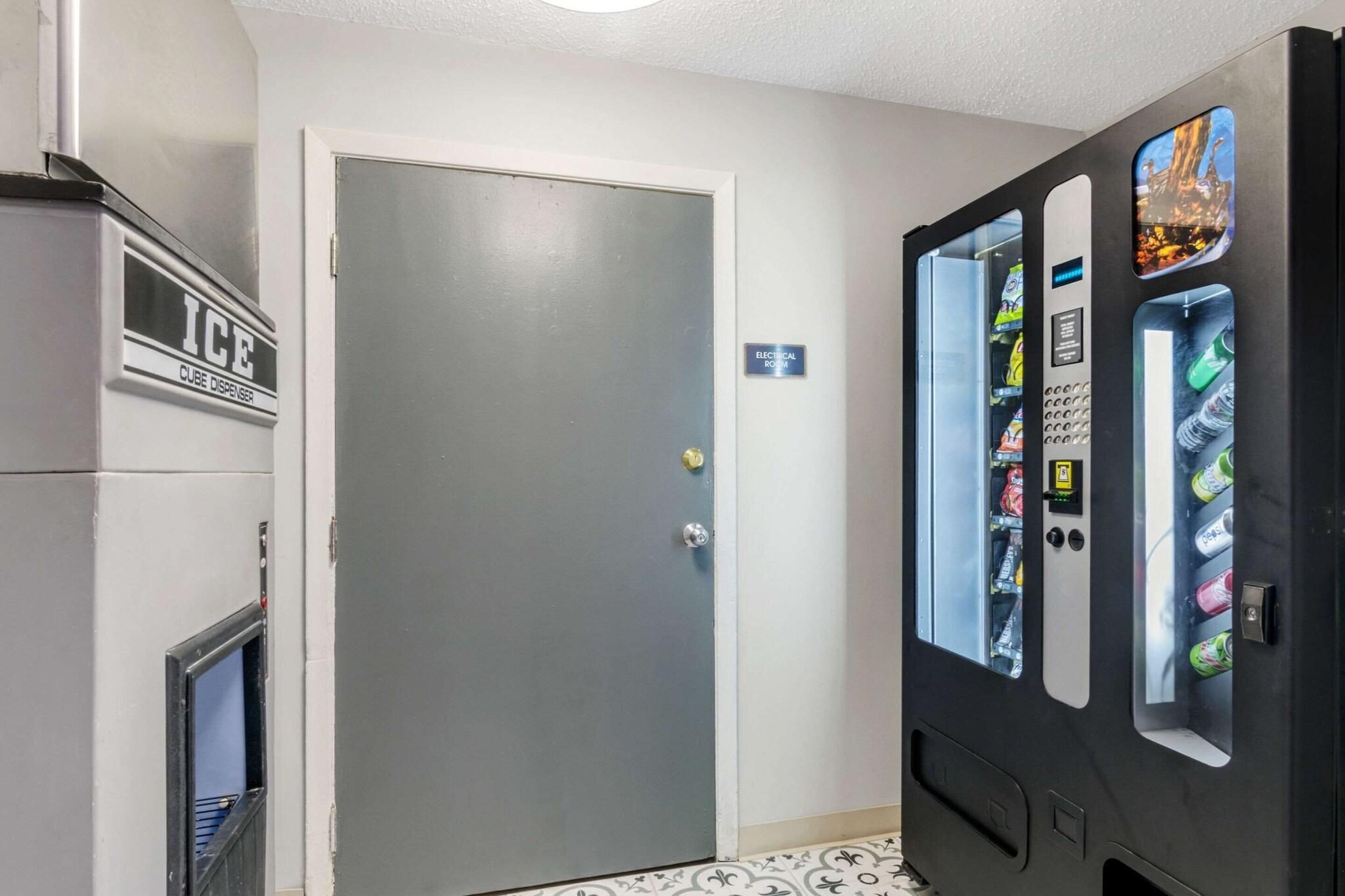 Máquina de vendas com diversas opções de bebidas, porta com dispensador de gelo e um aviso 'ELÉTRICO' na parede.