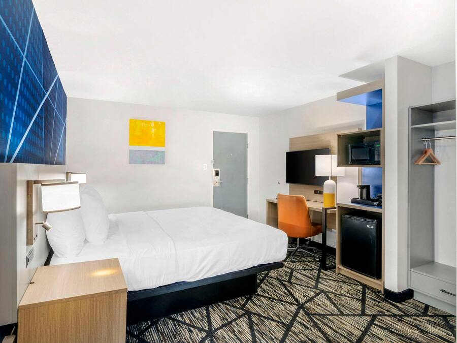 Quarto de hotel com cama, escrivaninha, cadeira, TV e micro-ondas.