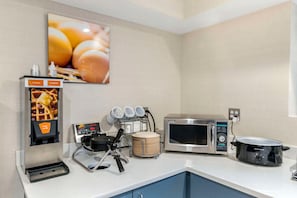 Uma cozinha compacta equipada com máquina de waffles, cafeteira, micro-ondas e panela de cozimento lento.