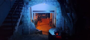 Entrada de um edifício com arco de pedra, uma escadaria à esquerda e interior iluminado em vermelho visível pelo arco.