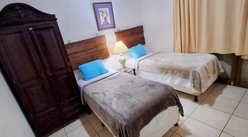 Quarto com duas camas, um guarda-roupa de madeira, uma mesa de cabeceira com abajur e um quadro na parede.
