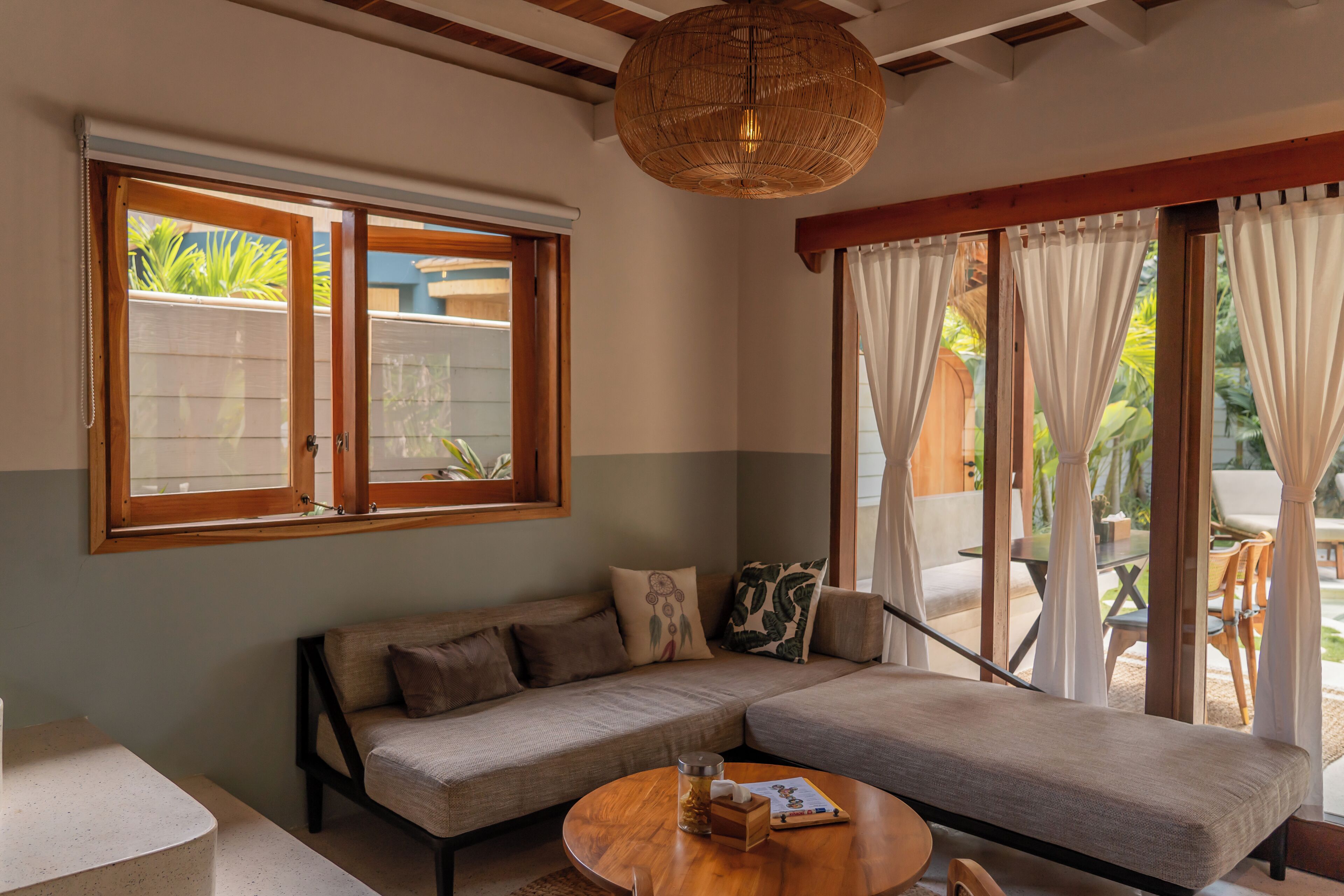 Uma sala de estar moderna com sofá seccional, mesa de centro de madeira redonda e grandes janelas com cortinas.