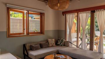 Uma sala de estar moderna com sofá seccional, mesa de centro de madeira redonda e grandes janelas com cortinas.