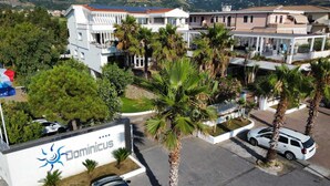 A building with a sign reading "Dominicus," surrounded by palm trees and parked cars.