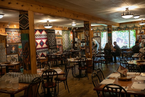 Restaurante com interior em madeira, várias mesas e cadeiras, e diversas decorações nas paredes.