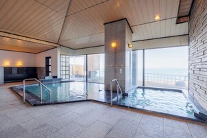 Piscina interna moderna com paredes de vidro transparente, teto alto e um pilar de pedra.