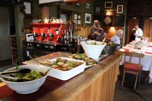 Buffet com diversos pratos, uma máquina de café e um alvo de dardos ao fundo.