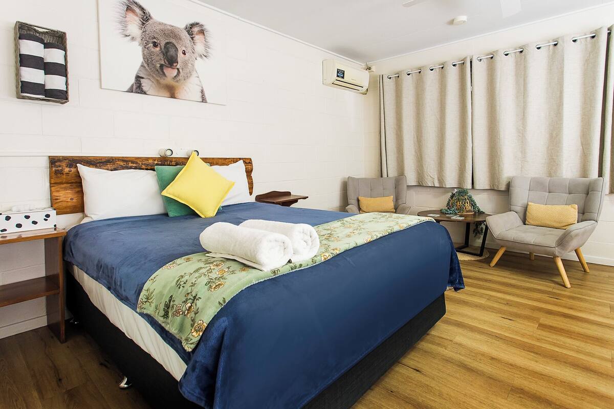 Quarto de hotel com uma cama, uma cadeira, uma mesa de cabeceira, ar condicionado fixado na parede e uma cortina.