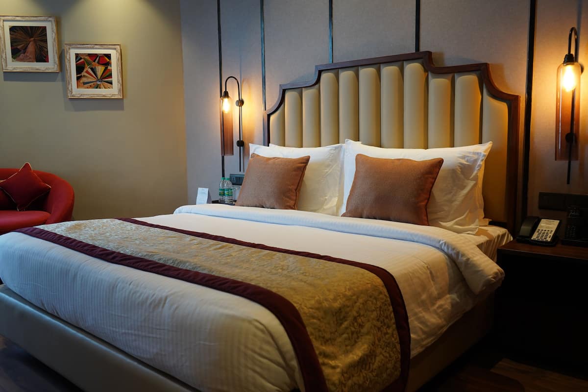Quarto de hotel com uma cama grande, mesa de cabeceira com telefone e uma cadeira vermelha.