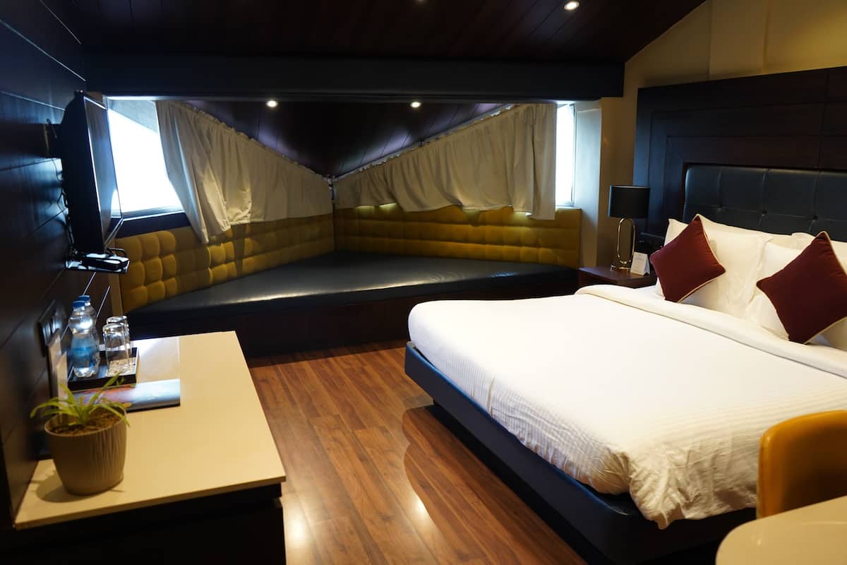Quarto moderno com uma cama grande, área de estar e uma mesinha com uma planta.