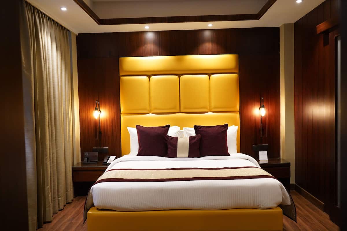 Quarto de hotel com uma cama grande, cabeceira de madeira e duas mesas de cabeceira com luminárias.